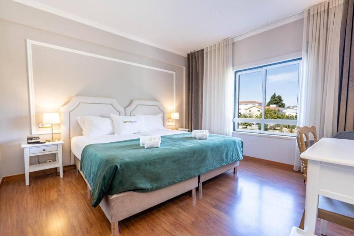 Quarto de hotel com cama, mesas de cabeceira, janela e uma cadeira.