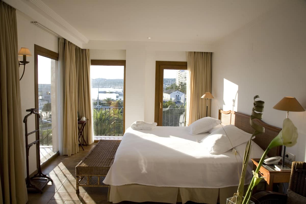 Quarto de hotel com uma cama grande, vista da cidade e varanda com uma cadeira de vime.