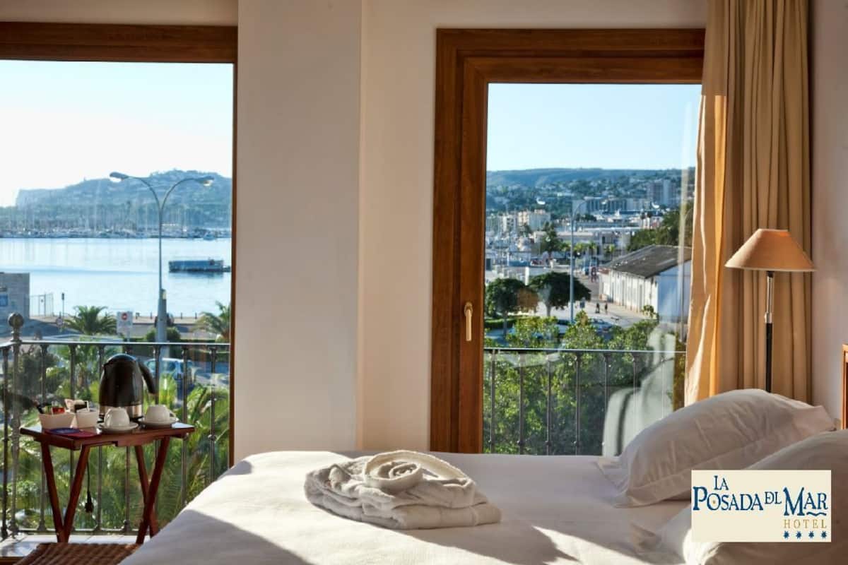 Quarto de hotel com uma cama, uma mesa com itens de café da manhã e vista para a cidade e para a água.