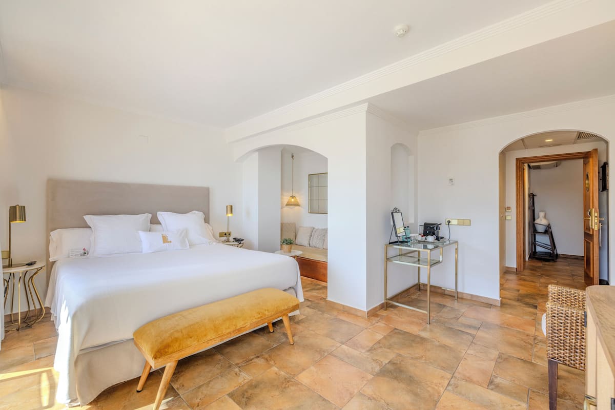 Quarto de hotel com uma cama grande, uma escrivaninha e um banco.
