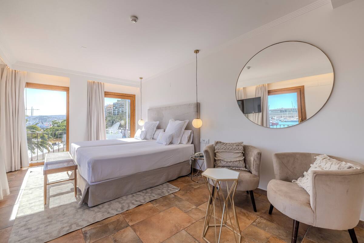 Quarto moderno com uma cama grande, um espelho redondo, área de estar e vista da cidade.