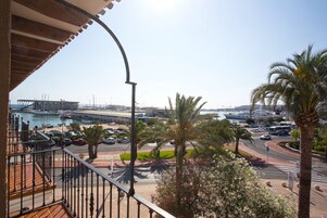 Uma varanda com vista para um porto, palmeiras e uma estrada com veículos.