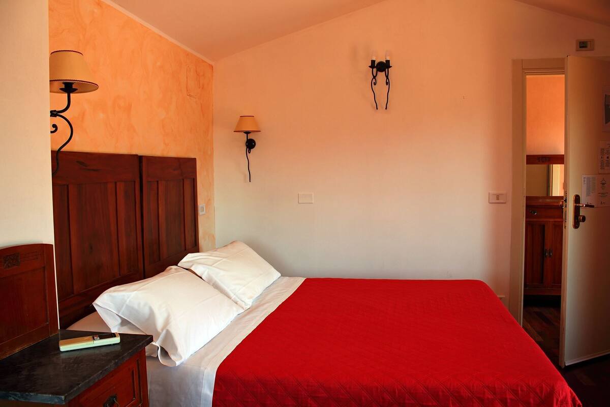 Quarto com cama, mesa de cabeceira, guarda-roupa de madeira e duas luminárias na parede.