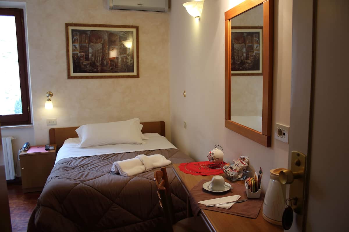 Quarto de hotel com cama, escrivaninha com cadeira, espelho e um quadro na parede.