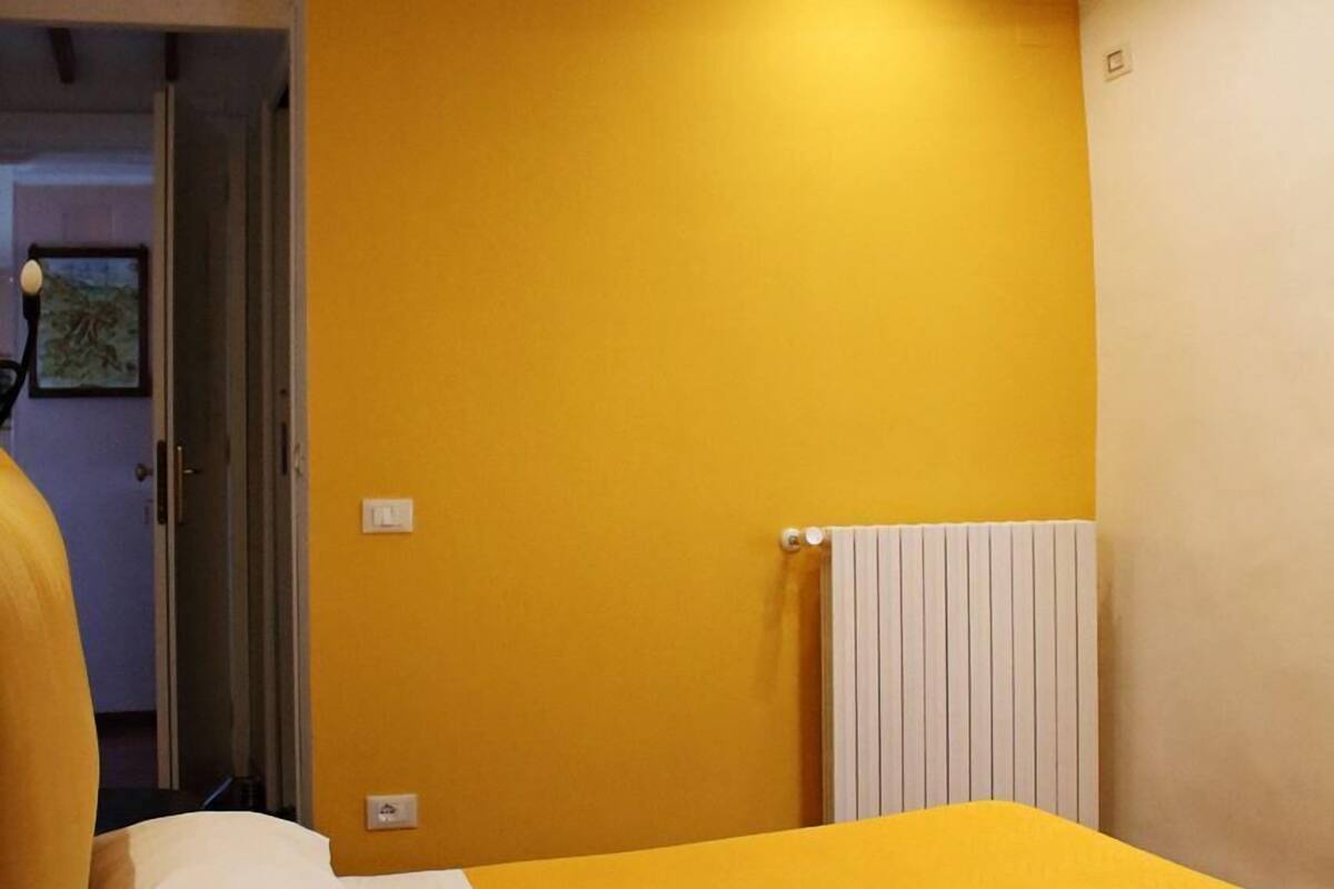 Quarto com uma cama, um radiador e uma porta que dá para outro espaço.