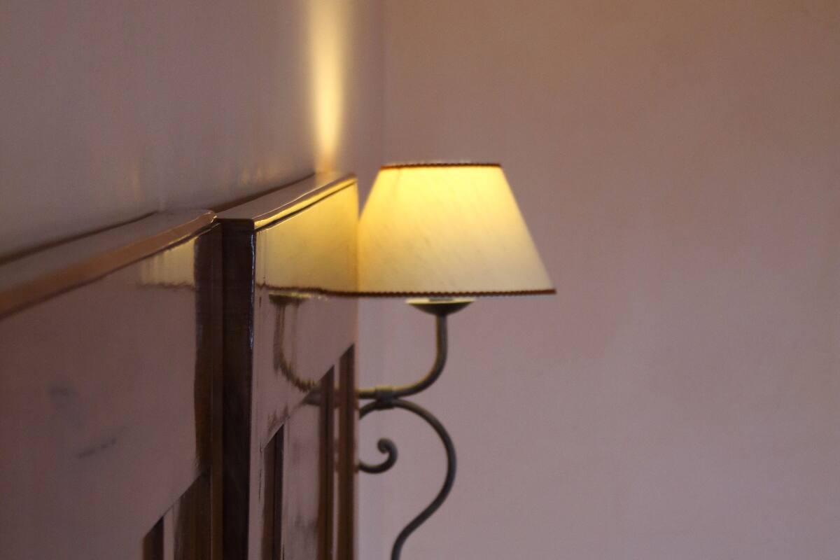 Canto de um quarto com uma luminária, uma cadeira e uma parede.