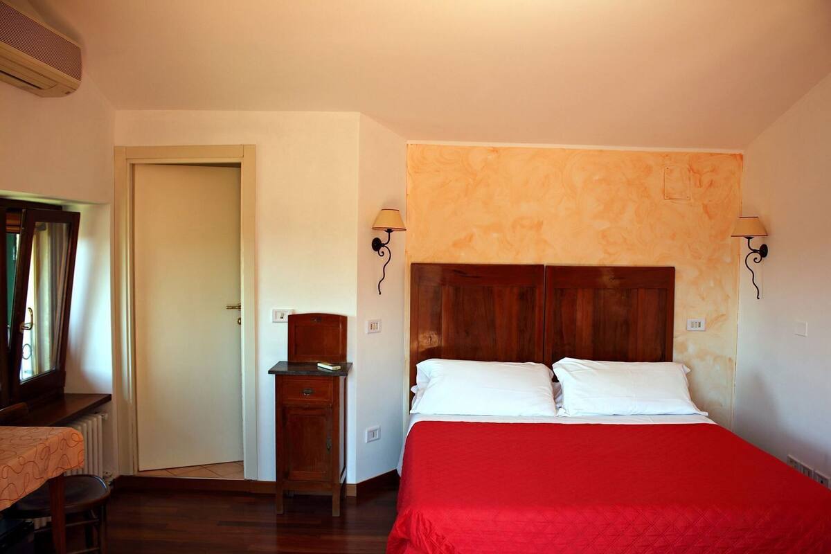 Quarto com cabeceira de madeira, colcha vermelha, escrivaninha com cadeira e espelho.