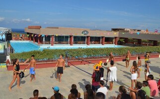 Uma área à beira da piscina com espaço para espectadores, um palco e um edifício com uma placa.
