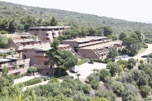 Um hotel de vários andares com design de telhado plano, rodeado por vegetação e colinas.