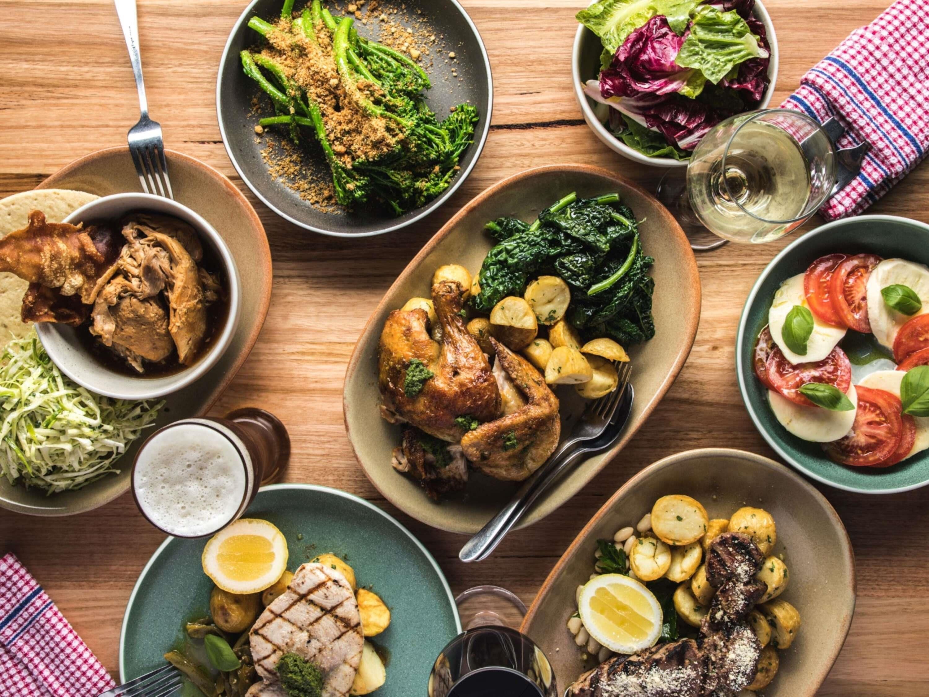Diversos pratos, incluindo frango assado, legumes e uma salada, sugerindo um ambiente de refeição.