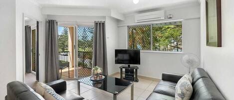 Uma sala de estar moderna com sofá, mesa de centro, televisão e varanda com cortinas.