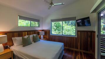Quarto com cama, mesas de cabeceira, ventoinha no teto, duas janelas e televisão fixada na parede.
