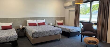 Quarto de hotel com uma cama grande, duas camas menores, uma cadeira, uma mesa e um ventilador de teto.