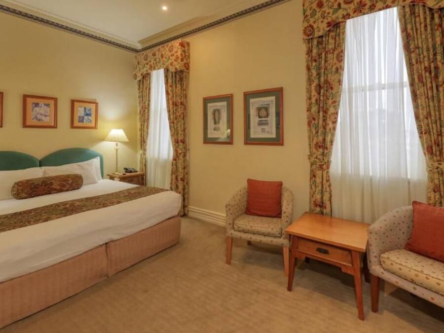 Quarto de hotel com cama, duas cadeiras, uma mesa e quadros nas paredes.
