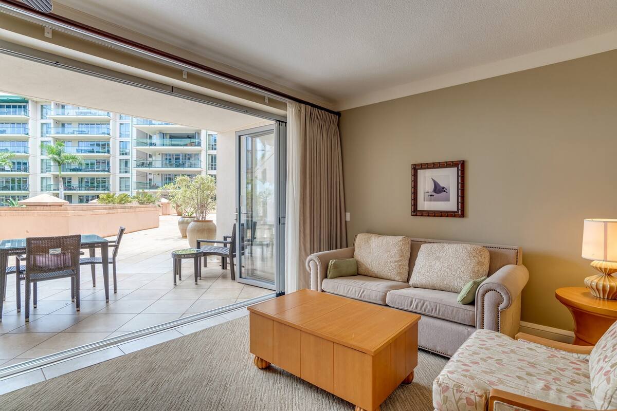 Quarto de hotel moderno com porta de vidro deslizante que dá para um pátio externo, mobiliado com sofá, poltrona e mesa de centro de madeira.
