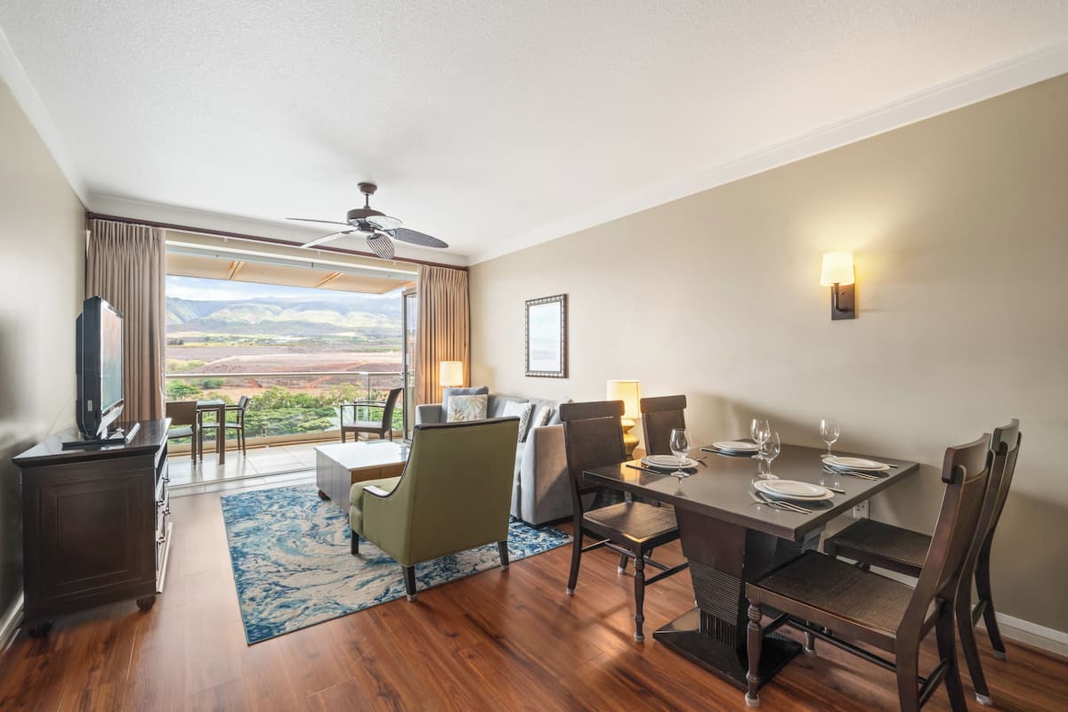 Quarto de hotel com área de jantar, televisão e uma grande janela com vista para as montanhas.