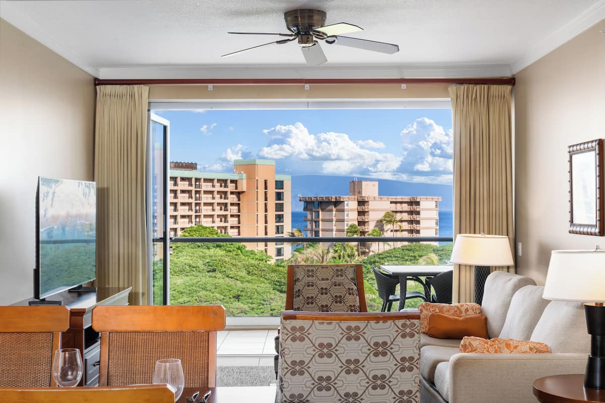 Quarto de hotel com varanda, televisão, sofá e mesa com abajur.