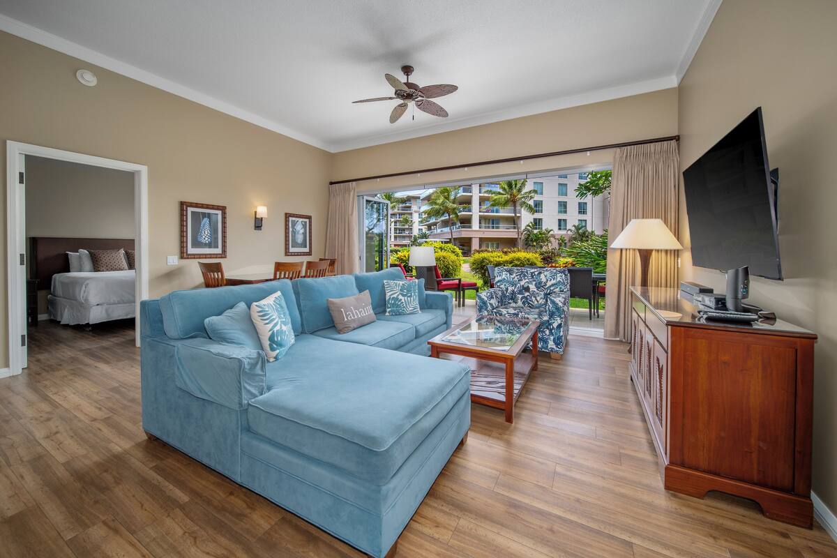 Uma sala de estar moderna com um sofá azul, uma mesa de centro de madeira e uma TV sobre um móvel de madeira.