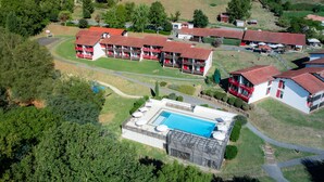 Vista aérea de um hotel com vários edifícios de telhado vermelho, uma piscina e vegetação ao redor.