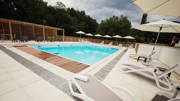 Piscina com espreguiçadeiras e guarda-sóis, cercada por um deck de madeira e uma área revestida com azulejos.
