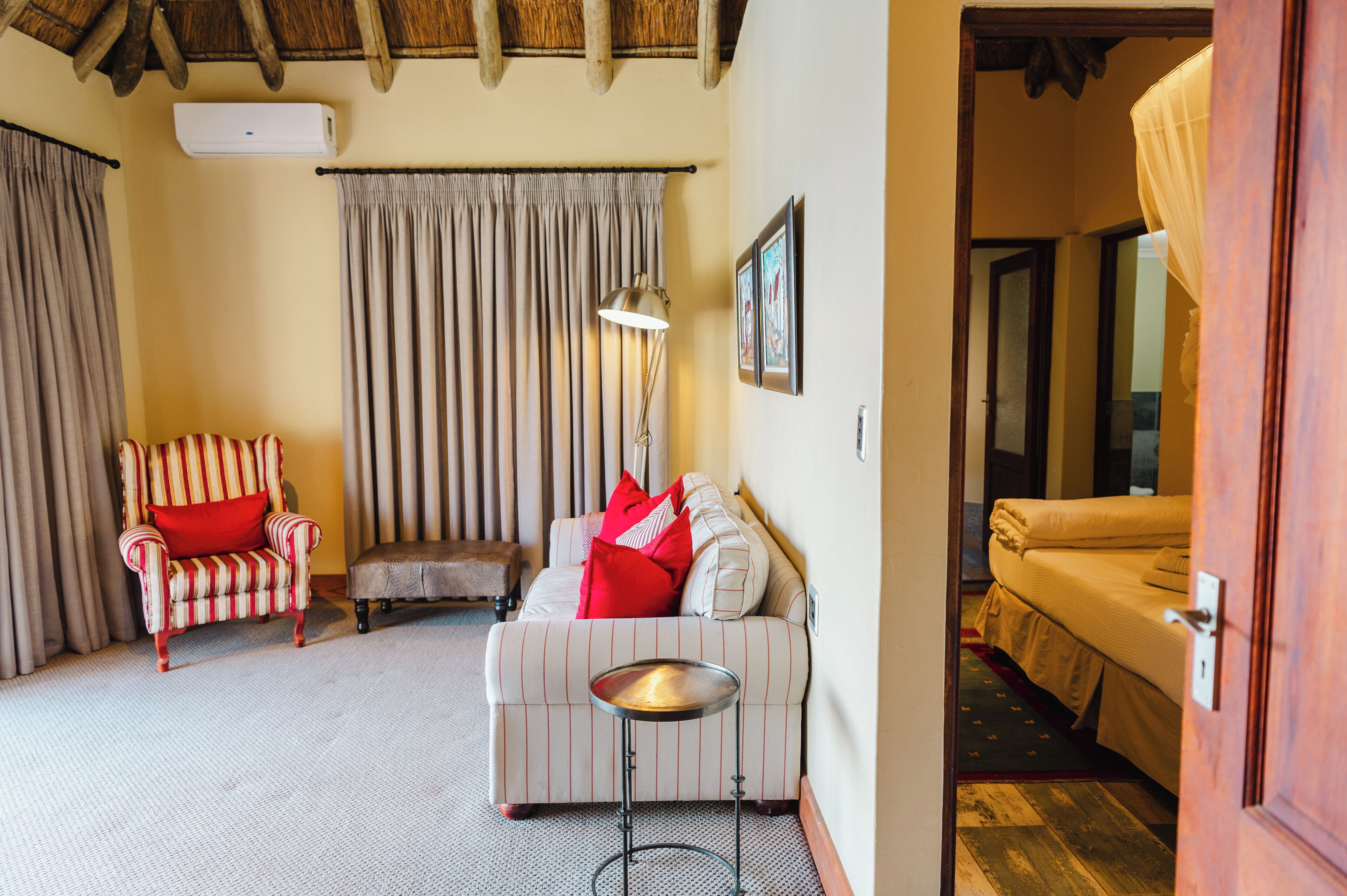 Quarto de hotel com um sofá listrado, uma poltrona listrada, uma mesa redonda pequena, uma cama e uma janela grande com cortinas.