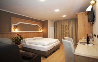 Quarto de hotel com cama, mesa de cabeceira, cadeira e televisão fixada na parede.