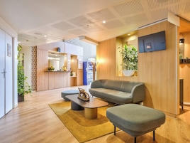 Um hall de hotel moderno com um sofá, mesa de centro e plantas em vasos.
