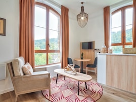 Quarto aconchegante com um sofá de vime, uma mesa redonda e vista para o verde através de grandes janelas.