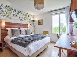 Quarto bem arrumado com uma cama grande, luminárias de cabeceira, cabeceira de madeira, uma escrivaninha e uma janela com vista.