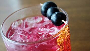 Um copo de bebida rosa com cubos de gelo e um toque de mirtilos e um pouco de pó de laranja.