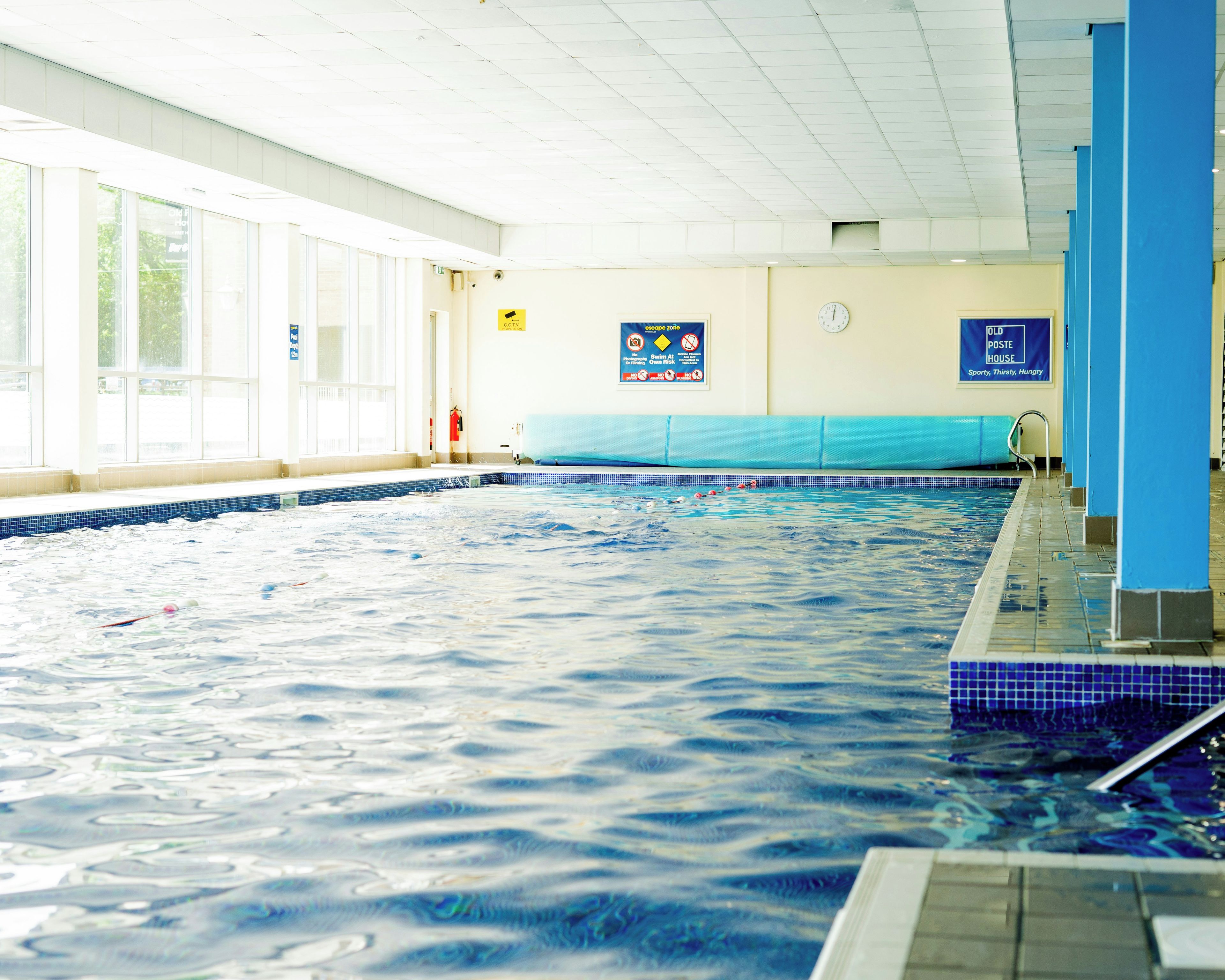 Piscina interior com água cristalina, deck azul e parede azul.