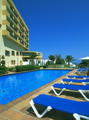 Um hotel com piscina, espreguiçadeiras e um céu azul límpido.