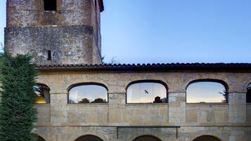 Um edifício histórico com uma torre de sino, janelas em arco, área de estar externa e um grande jardineira no pátio.
