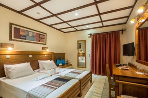 Quarto de hotel com cama de madeira, escrivaninha, espelho e teto com vigas de madeira.