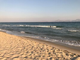 Uma praia de areia com ondas suaves e céu claro.