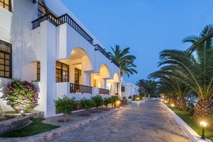 Um hotel com fachada branca, janelas em arco e um caminho pavimentado.