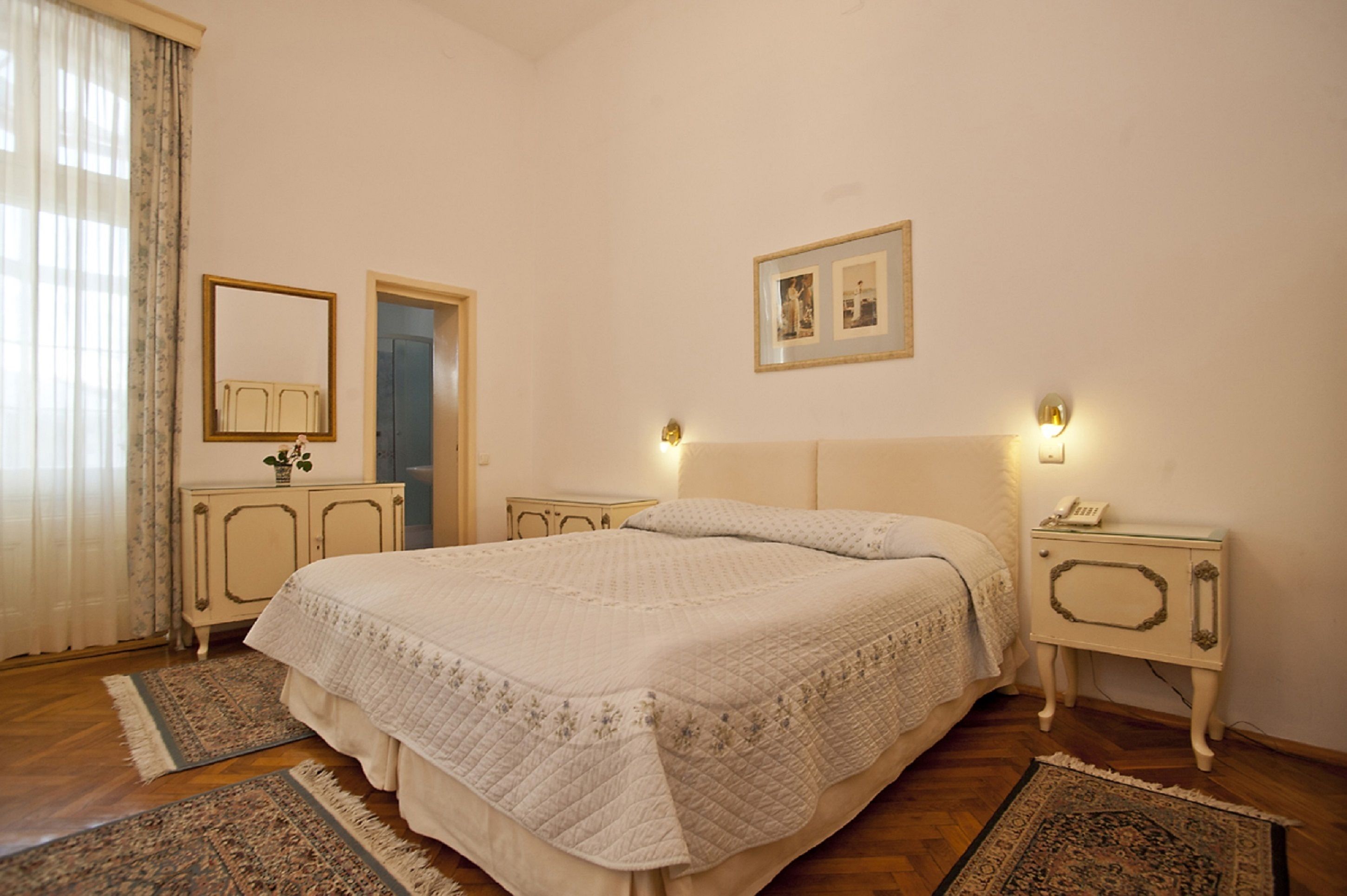 Quarto com uma cama grande, mesas de cabeceira, um espelho e um quadro na parede.