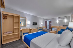 Quarto de hotel com cama, escrivaninha, cadeira, guarda-roupa e televisão.