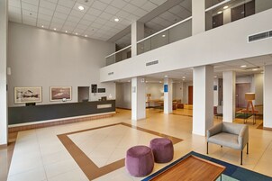 Um hall amplo com balcão de recepção, área de estar e teto alto com iluminação embutida.