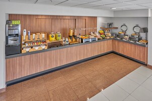 Uma área de buffet com estação de bebidas por autoatendimento, micro-ondas e diversas opções de comida.