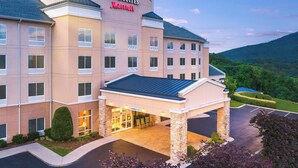 Um hotel Fairfield Inn & Suites Marriott com entrada desobstruída, estacionamento e área ajardinada com vista para as colinas ao redor.