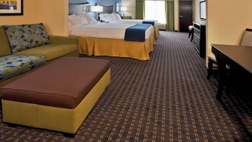 Quarto de hotel com cama, sofá, escrivaninha e televisão.