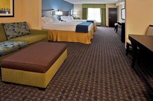 Quarto de hotel com cama, sofá, escrivaninha e televisão.