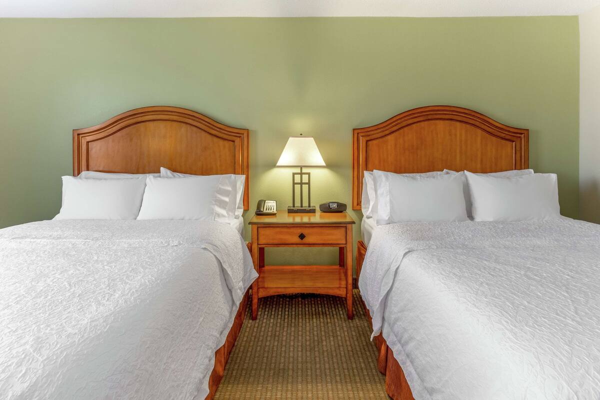 Quarto de hotel com duas camas, uma mesa de cabeceira com abajur e telefone.