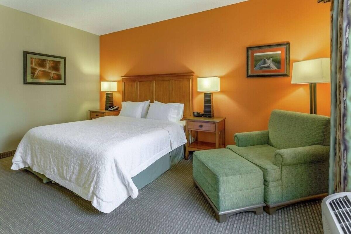 Quarto de hotel com cama, duas mesas de cabeceira, uma poltrona verde e duas luminárias fixadas na parede.