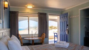 Quarto de hotel com cama, mesa de jantar, cadeira, televisão e porta para uma varanda com vista para a praia.