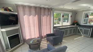 Sala de estar moderna com lareira, televisão e área de jantar, com cozinha ao fundo.