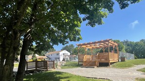 Um gazebo num parque com um caminho pavimentado e uma casa ao fundo.
