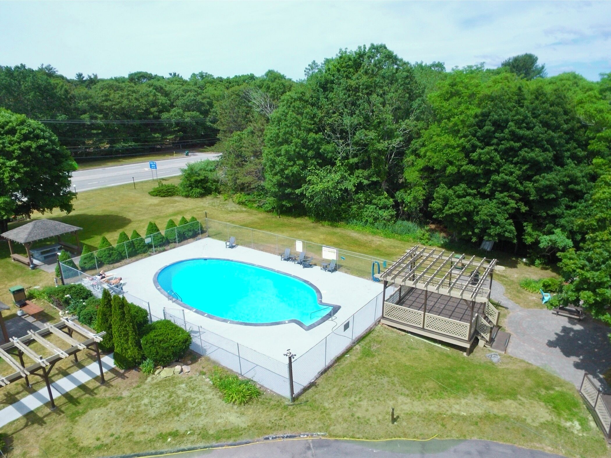 Uma piscina retangular com cerca ao redor, área de estar coberta e um gazebo.