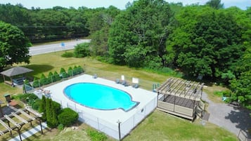 Uma piscina retangular com cerca ao redor, área de estar coberta e um gazebo.
